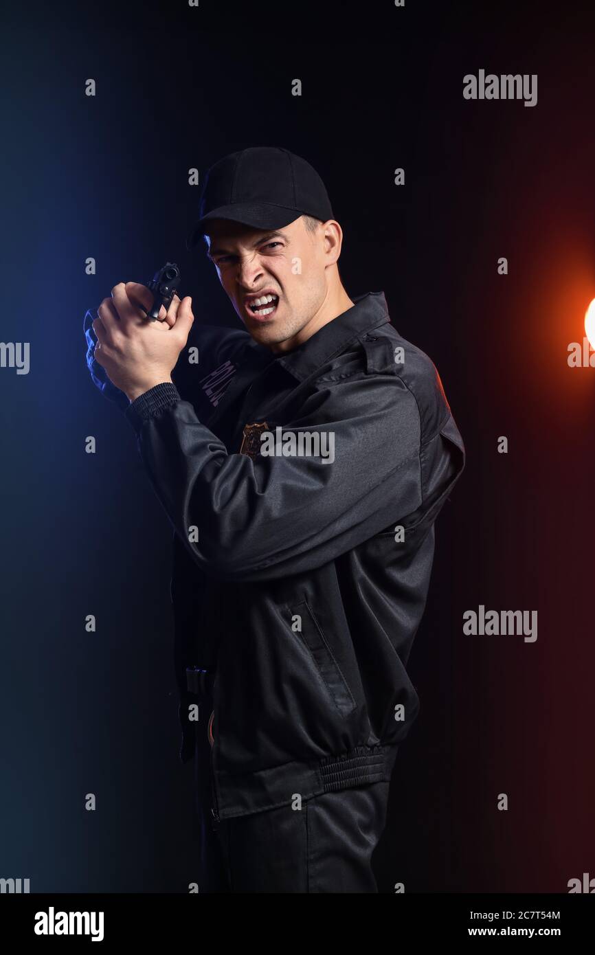 Aggressive police officer with gun on dark background Stock Photo - Alamy