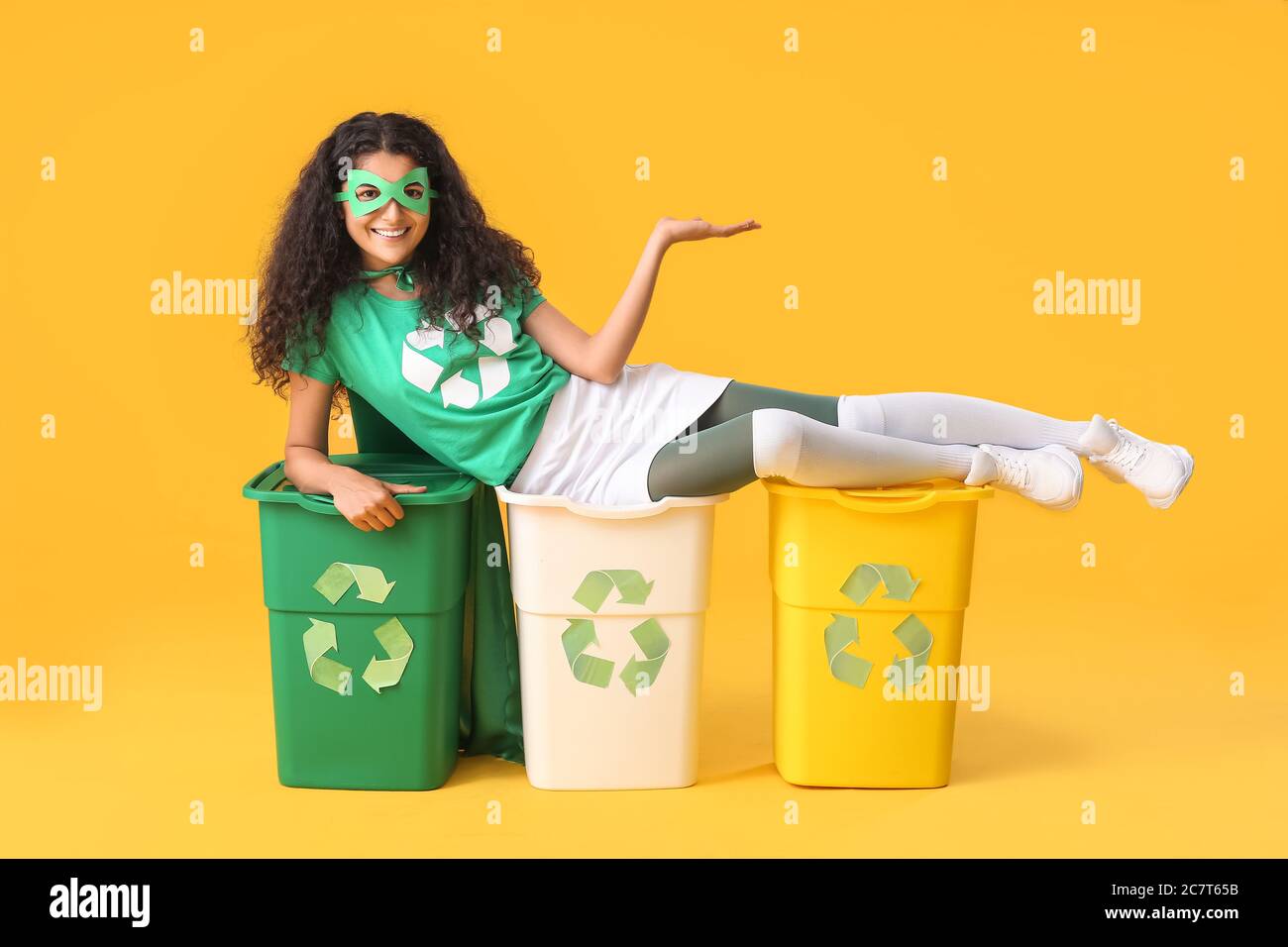 Woman dressed as eco superhero with trash bins on color background ...