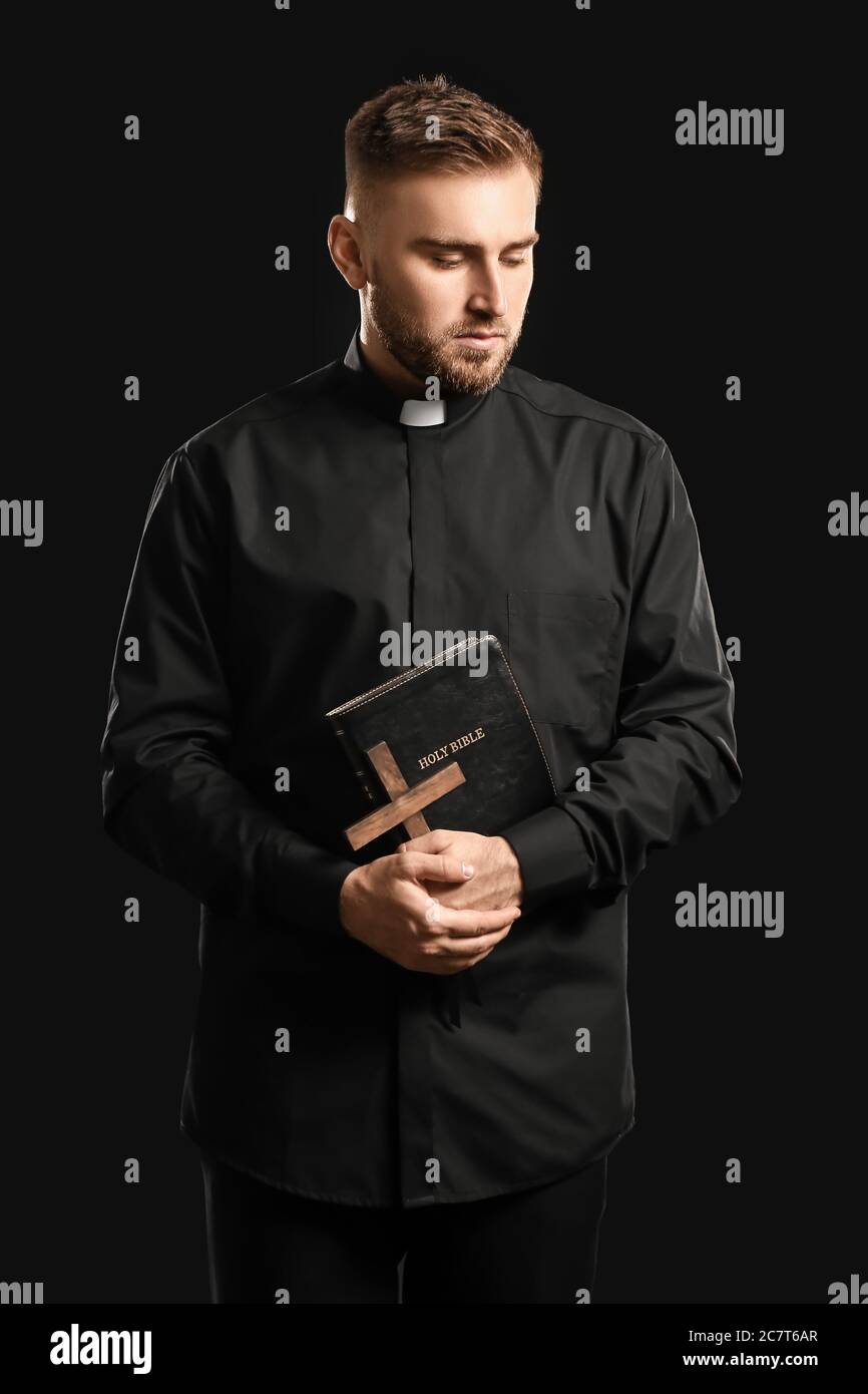 Young priest with Bible and cross on dark background Stock Photo - Alamy