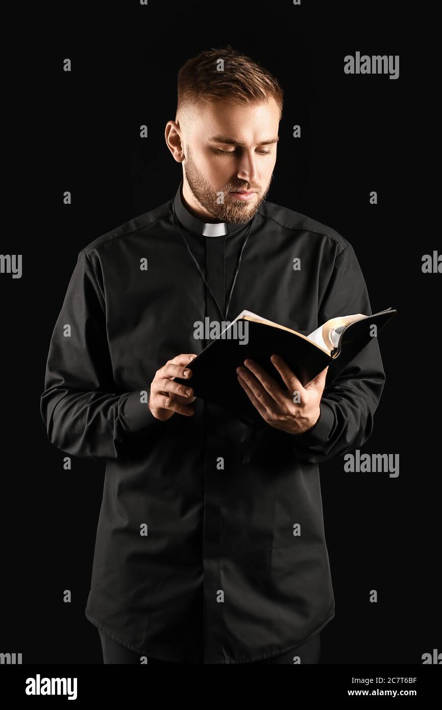 Young priest with Bible on dark background Stock Photo - Alamy