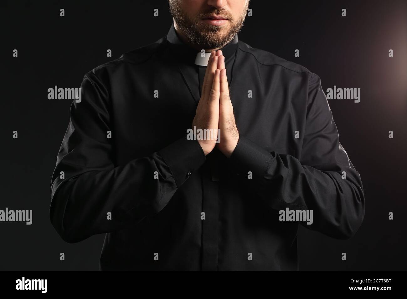Young priest praying to God on dark background Stock Photo - Alamy