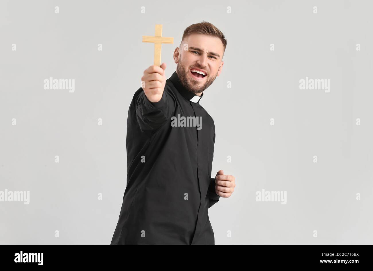 Emotional young priest with cross on light background Stock Photo - Alamy