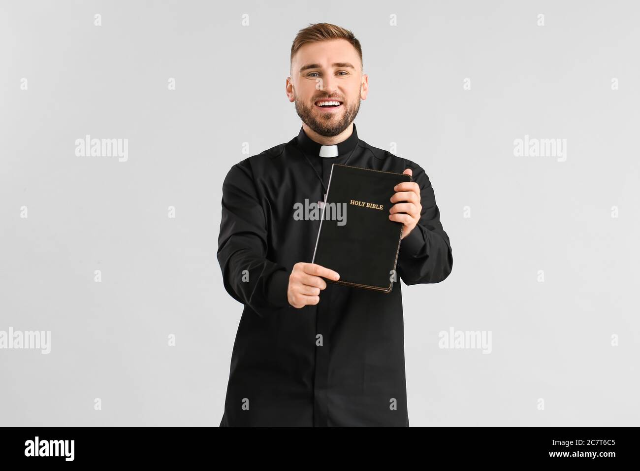Handsome young priest with Bible on light background Stock Photo - Alamy