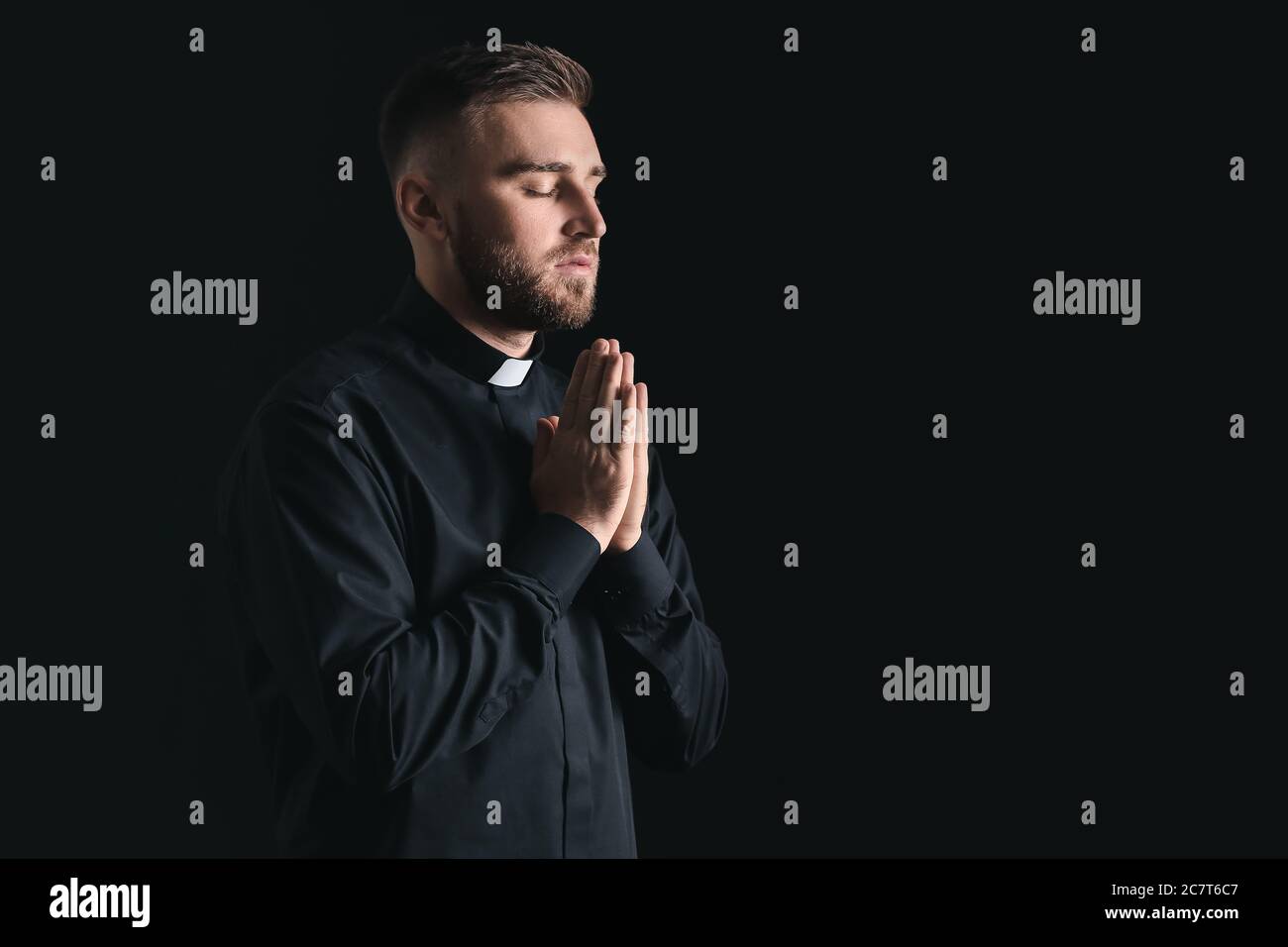 Young priest praying to God on dark background Stock Photo - Alamy