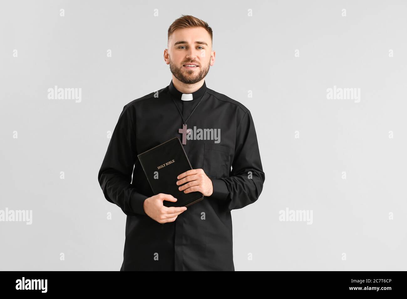 Handsome young priest with Bible on light background Stock Photo - Alamy