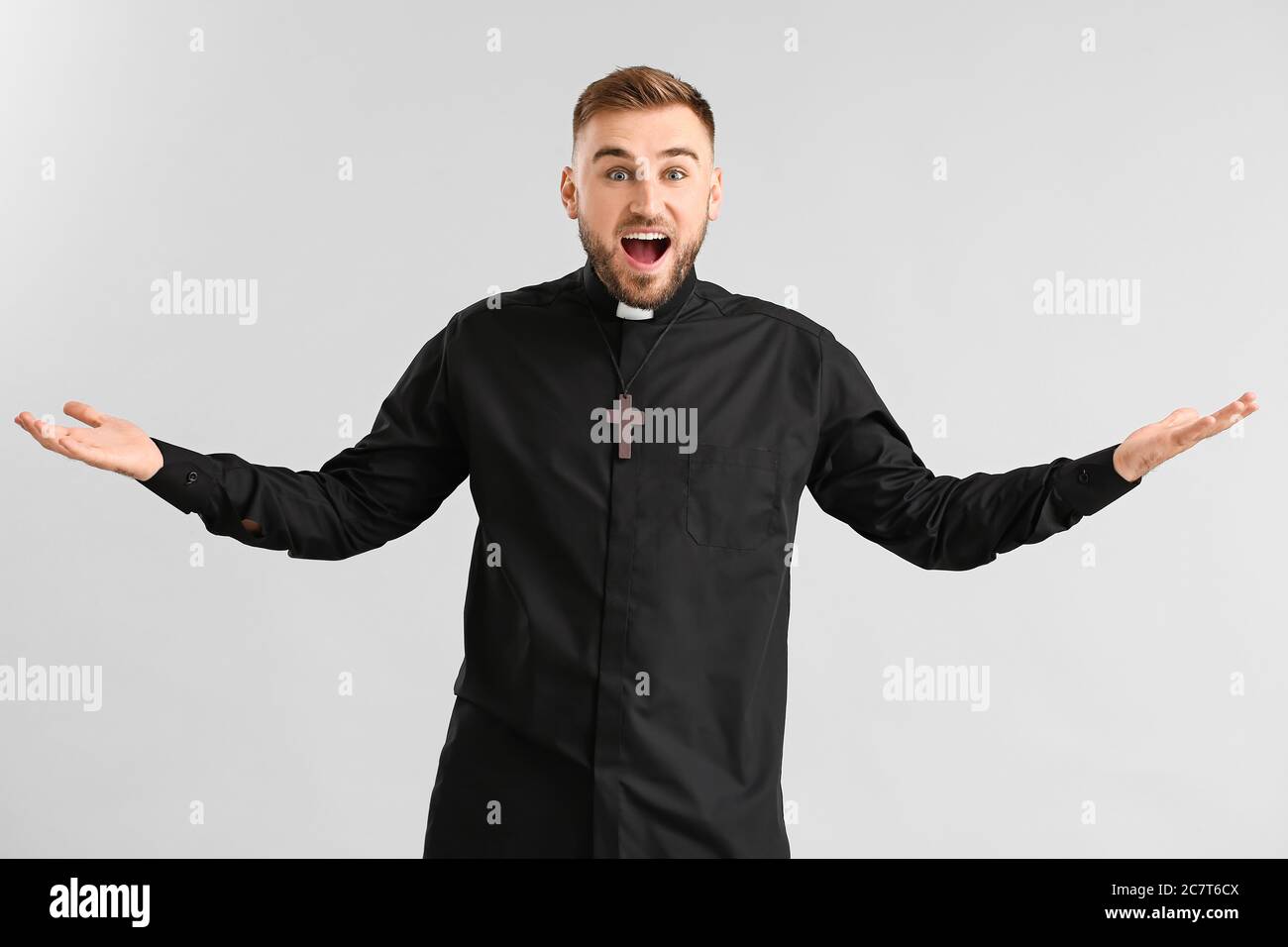 Surprised young priest on light background Stock Photo - Alamy