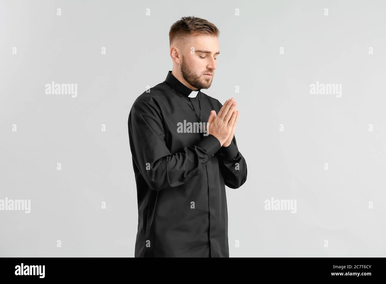 Young priest praying to God on light background Stock Photo - Alamy