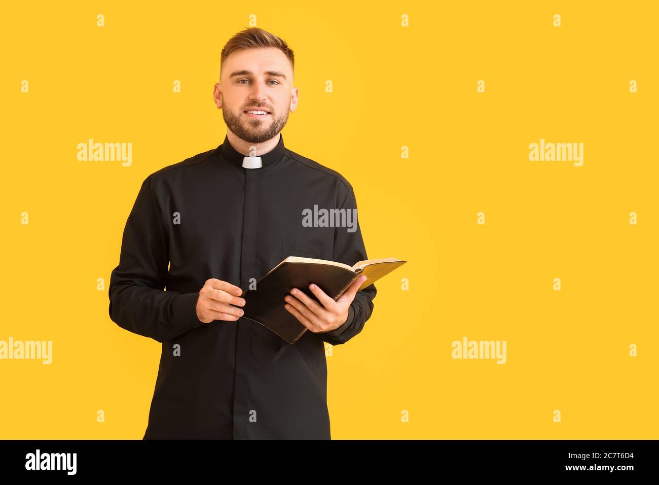 Handsome young priest with Bible on color background Stock Photo - Alamy
