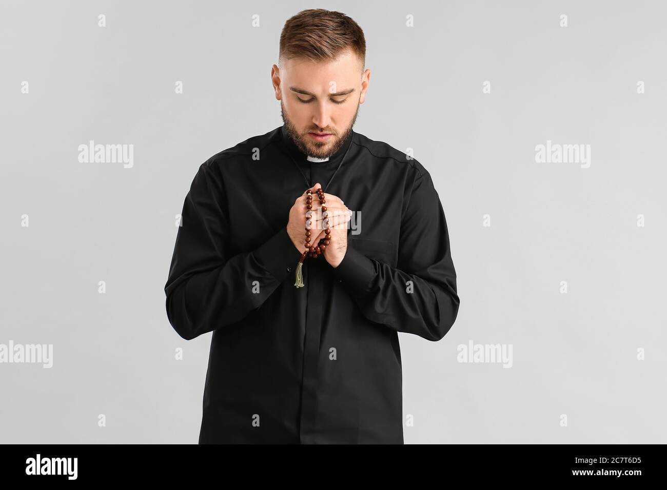 Young priest praying to God on light background Stock Photo - Alamy