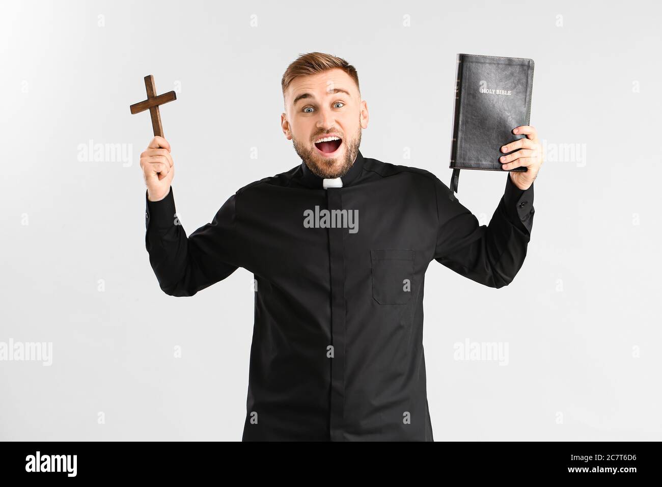 Surprised young priest with Bible and cross on light background Stock ...