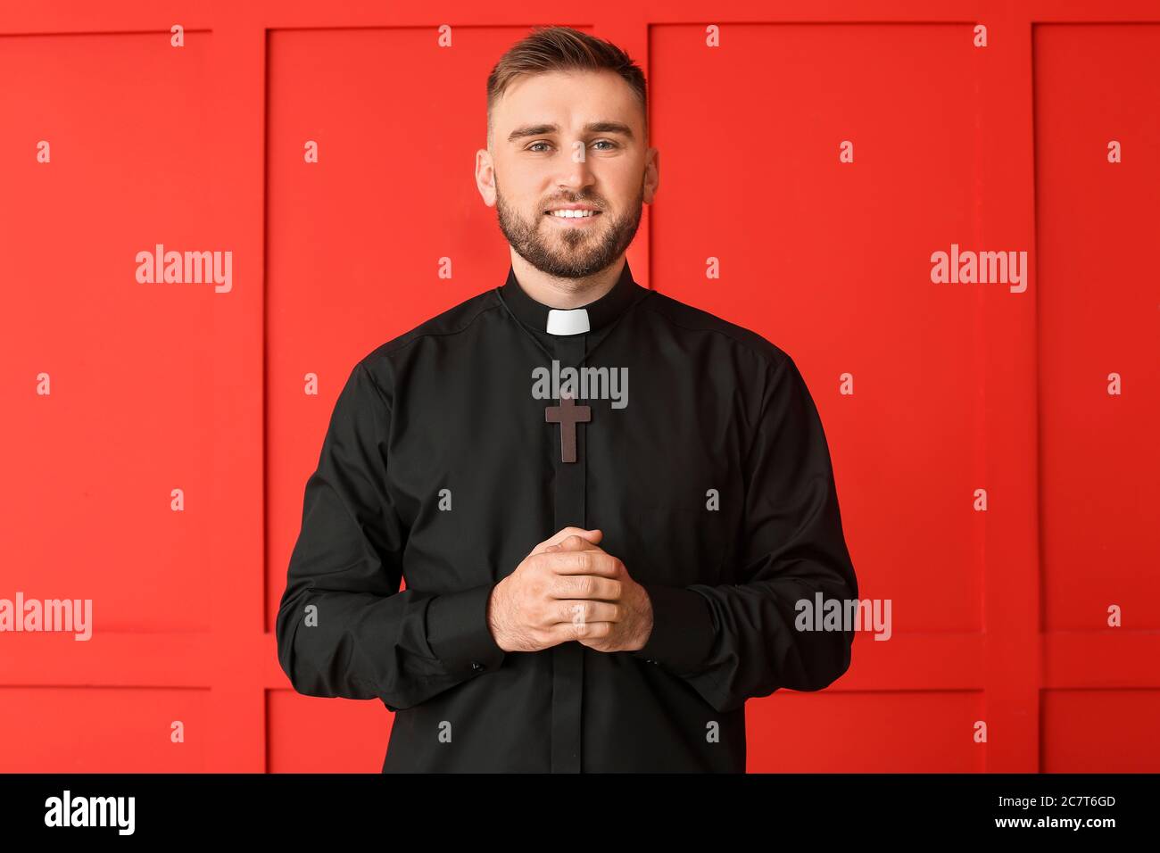 Handsome young priest on color background Stock Photo - Alamy