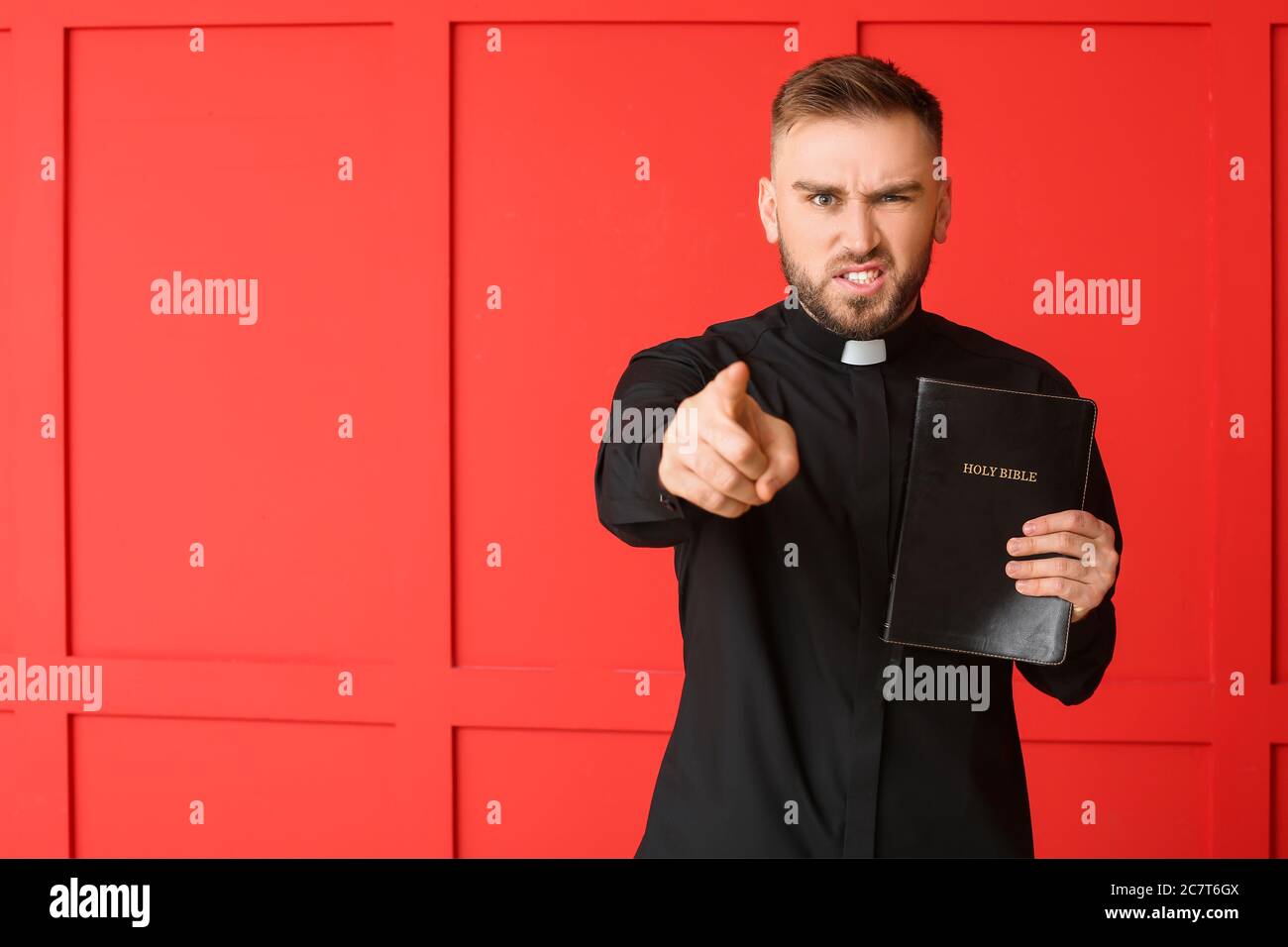 Angry young priest with Bible on color background Stock Photo - Alamy