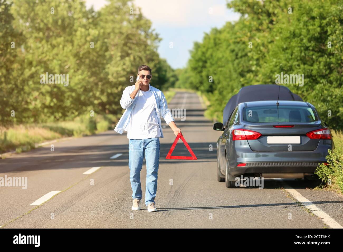 Young man with emergency stop sign near broken car on road Stock Photo ...