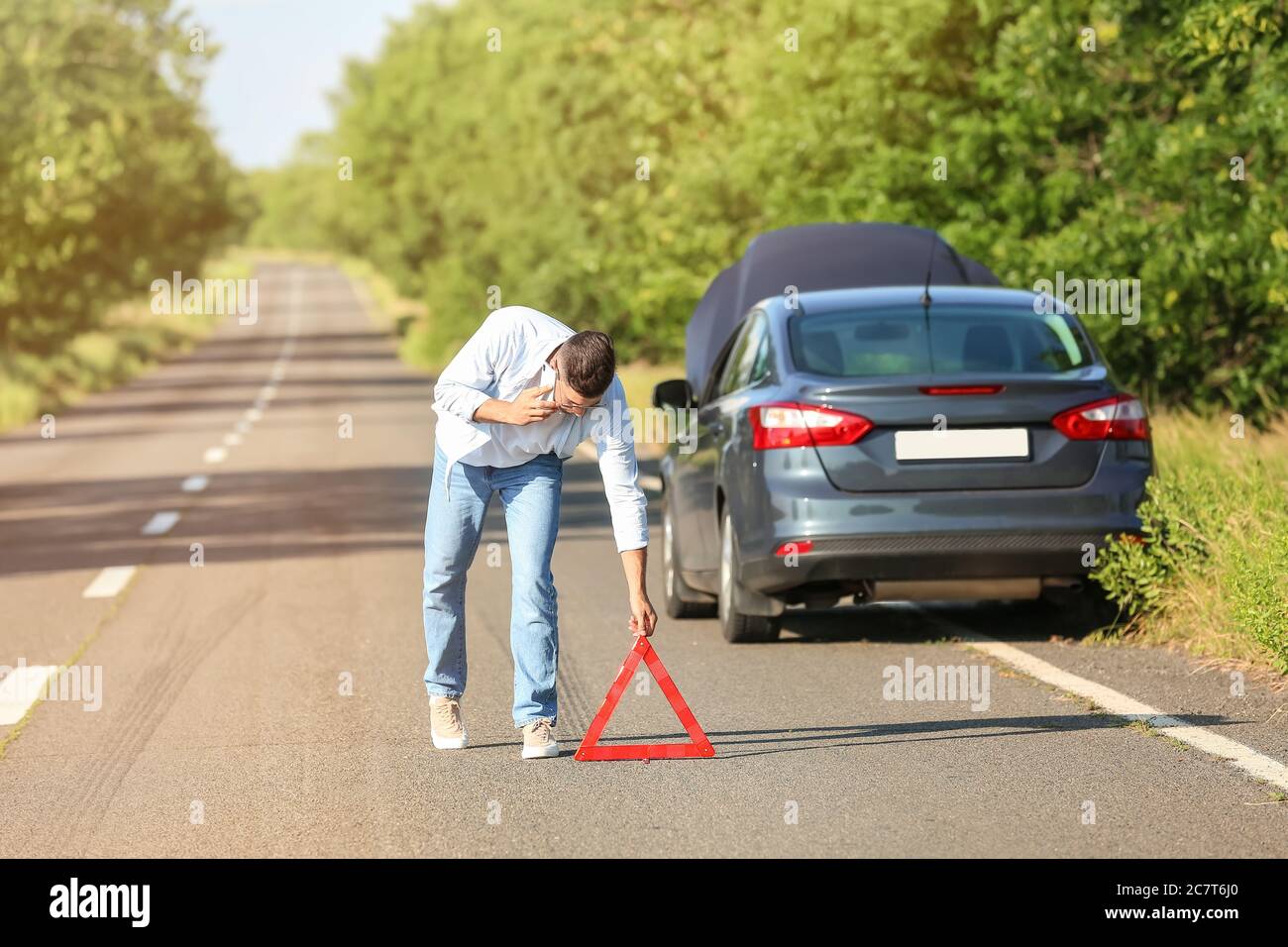 Young man with emergency stop sign near broken car on road Stock Photo ...
