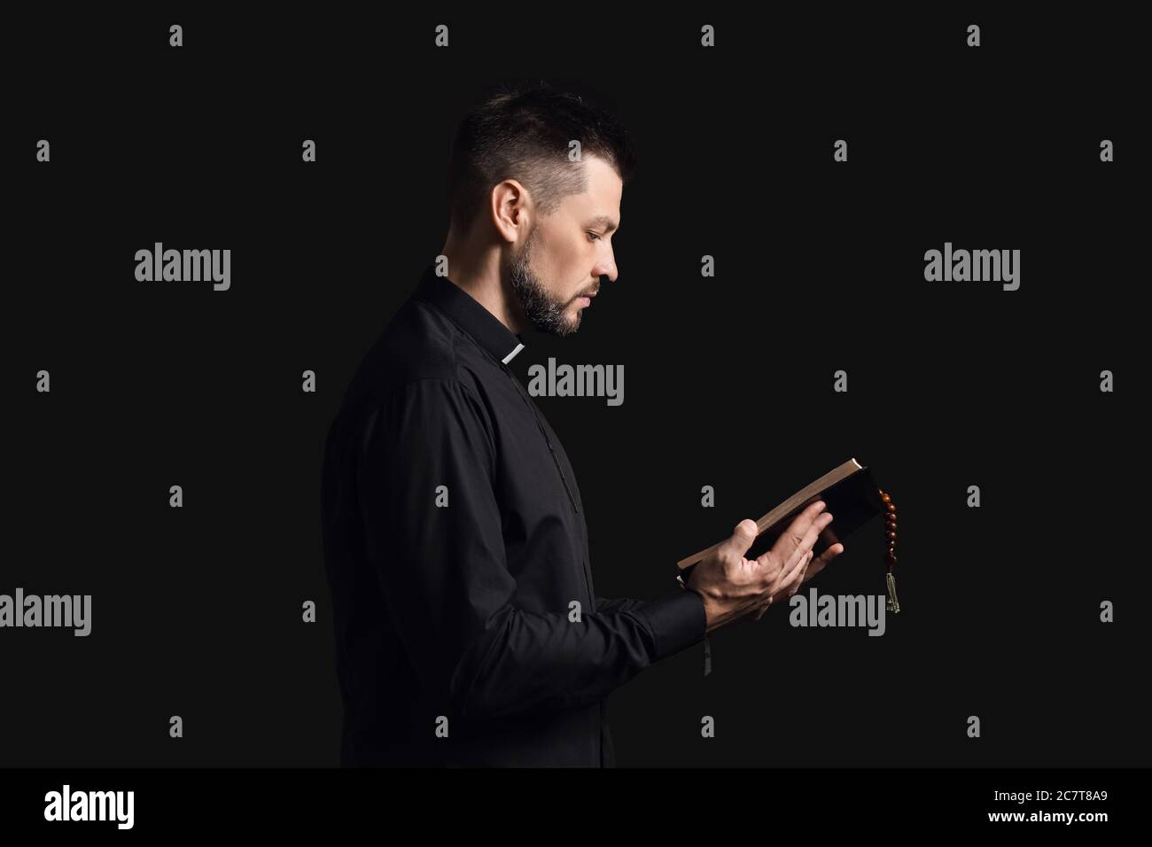 Handsome priest with Bible on dark background Stock Photo - Alamy