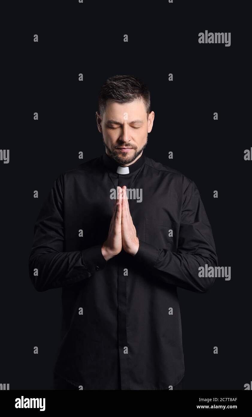 Handsome praying priest on dark background Stock Photo - Alamy