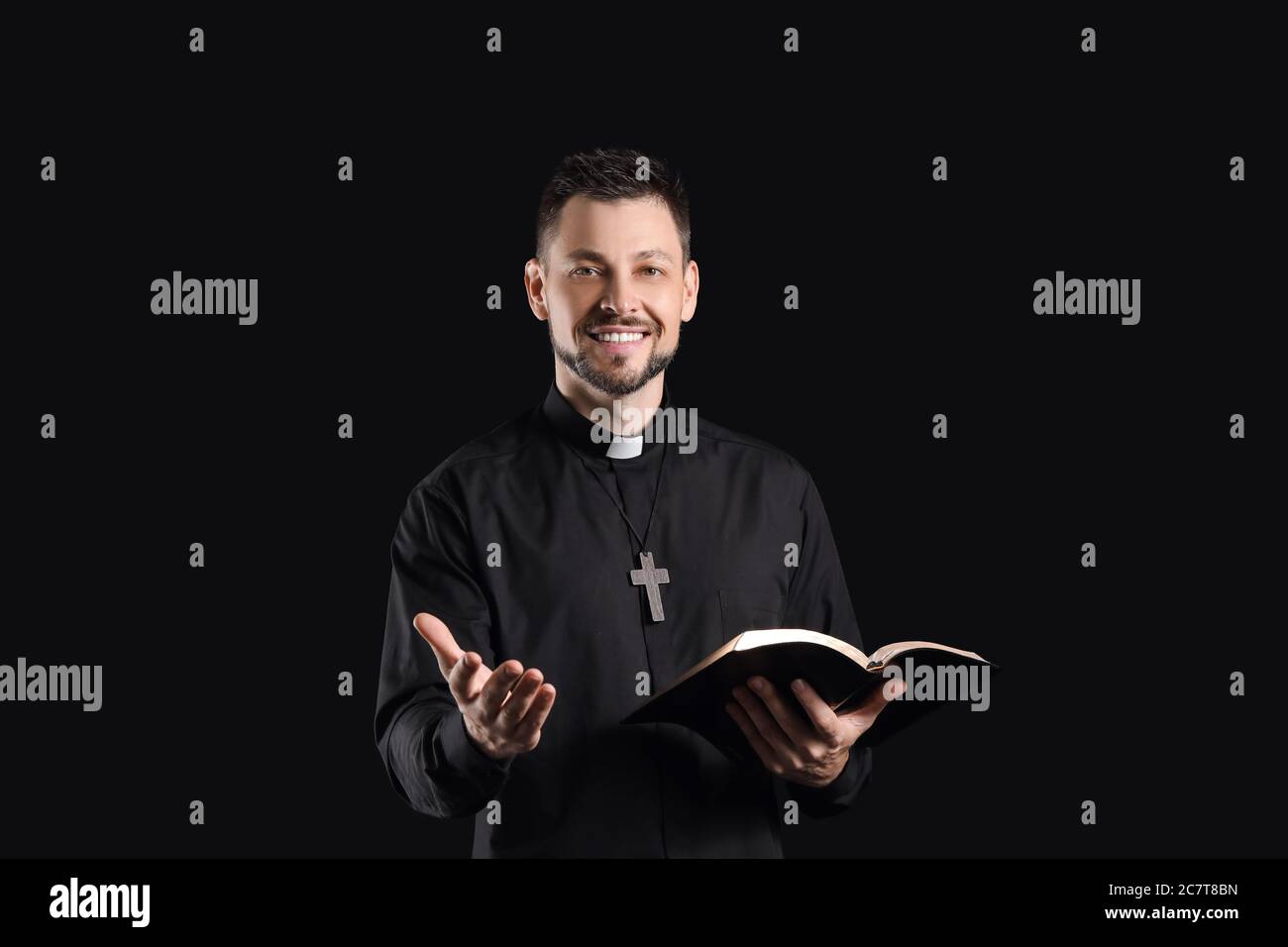 Handsome priest with Bible on dark background Stock Photo - Alamy