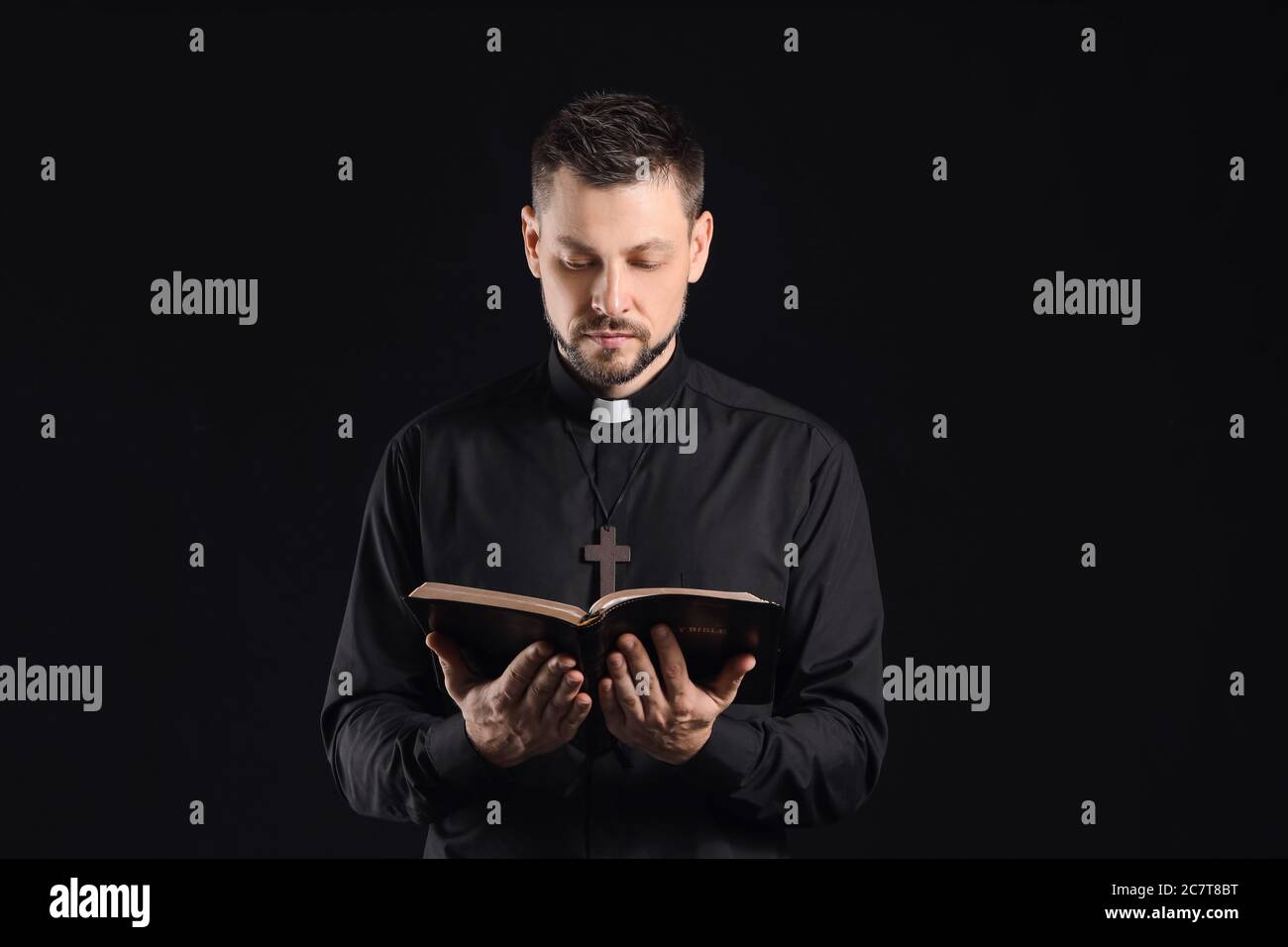 Handsome priest with Bible on dark background Stock Photo - Alamy