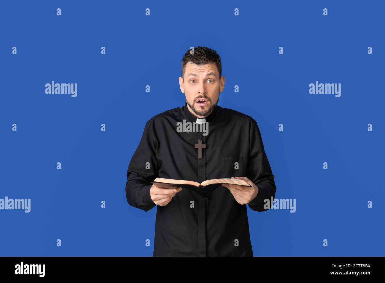 Shocked priest with Bible on color background Stock Photo - Alamy