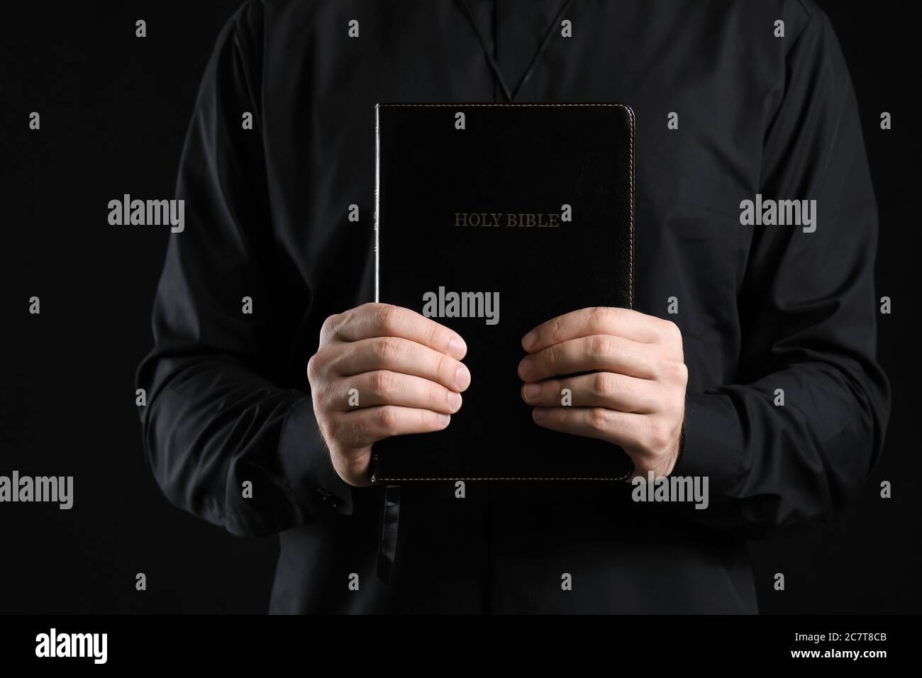 Handsome priest with Bible on dark background Stock Photo - Alamy