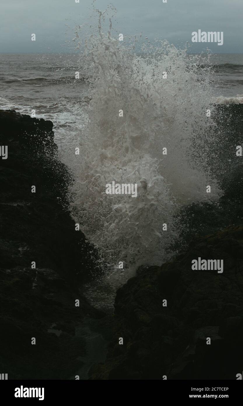 Vertical shot of splash of sea water waves hitting the rocky beach ...