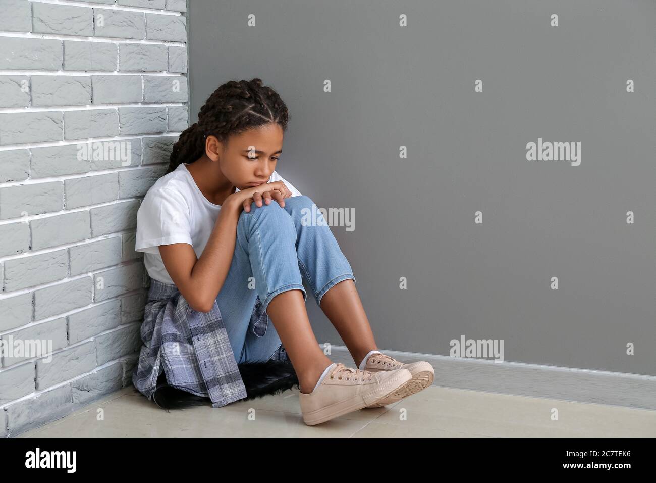 Sad African-American girl sitting near grey wall. Stop racism Stock ...