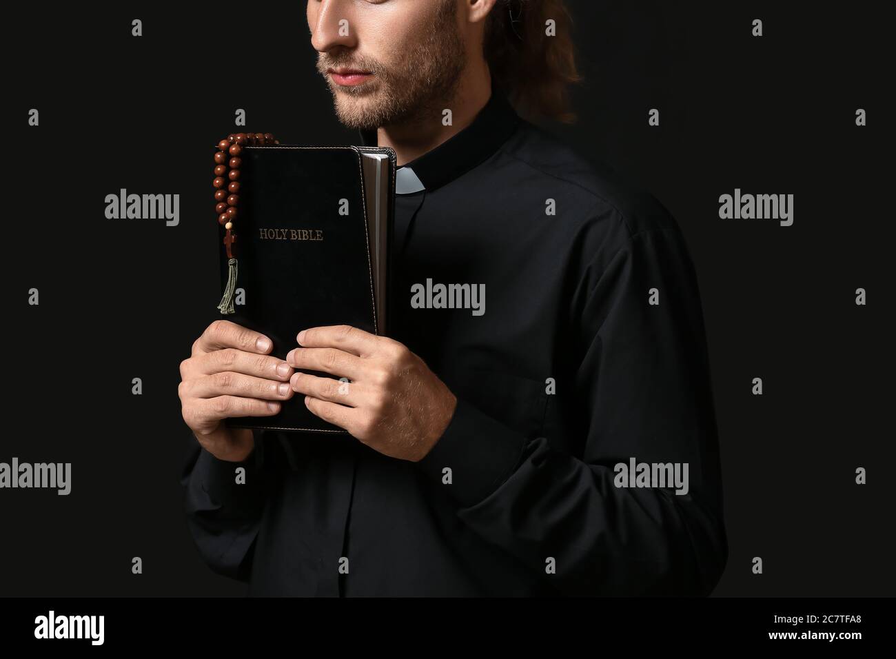 Handsome priest with Bible on dark background Stock Photo - Alamy