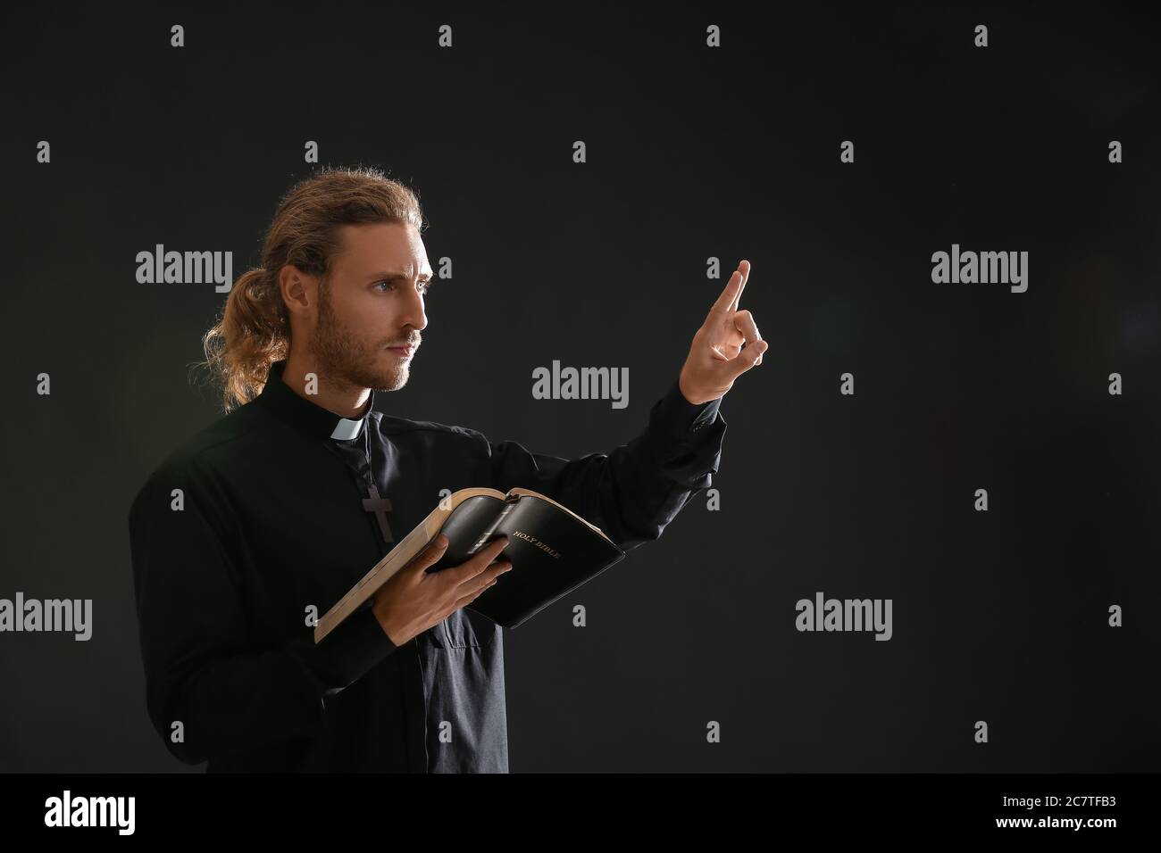 Handsome priest with Bible on dark background Stock Photo - Alamy