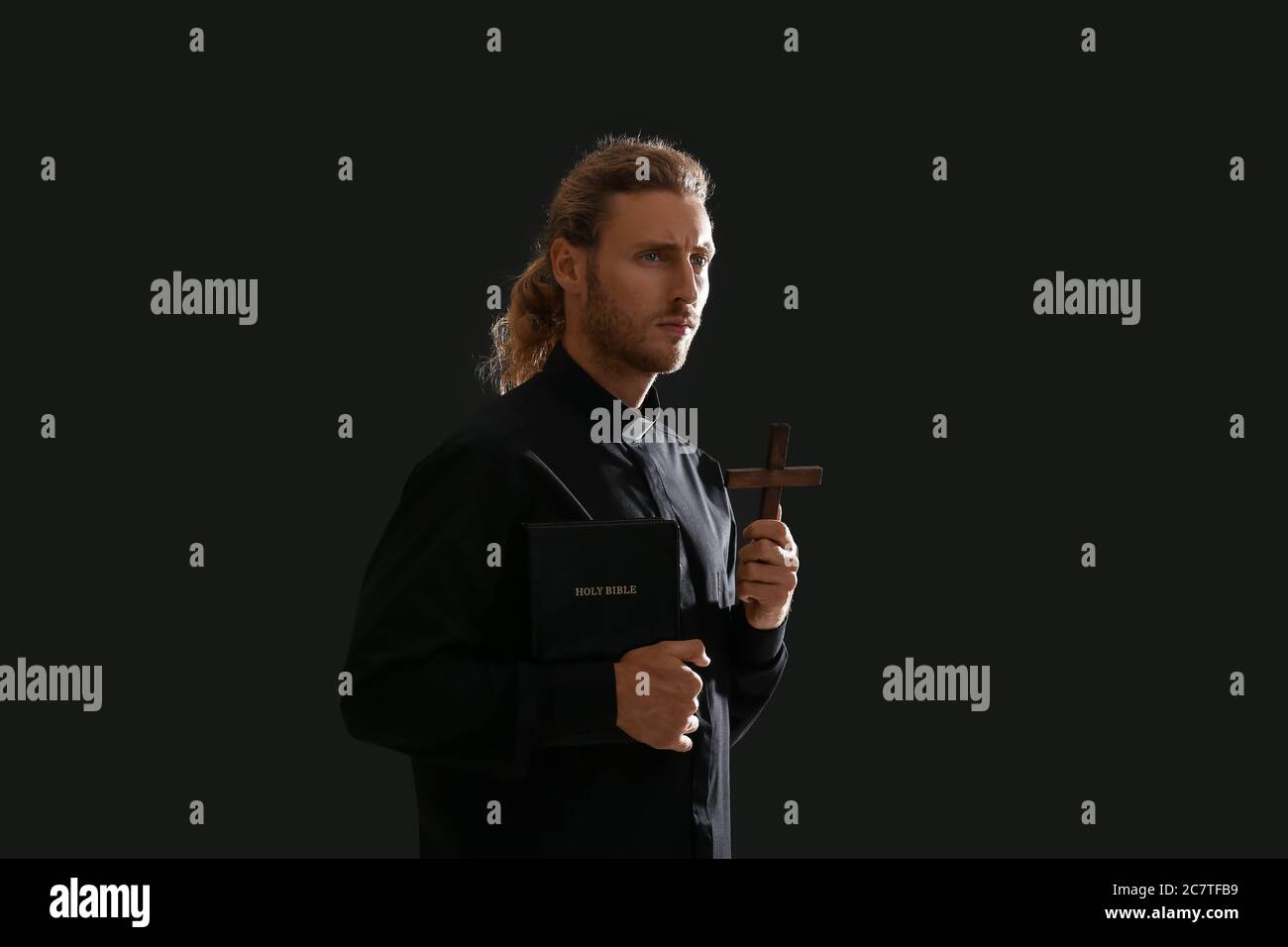 Handsome priest with Bible and cross on dark background Stock Photo - Alamy