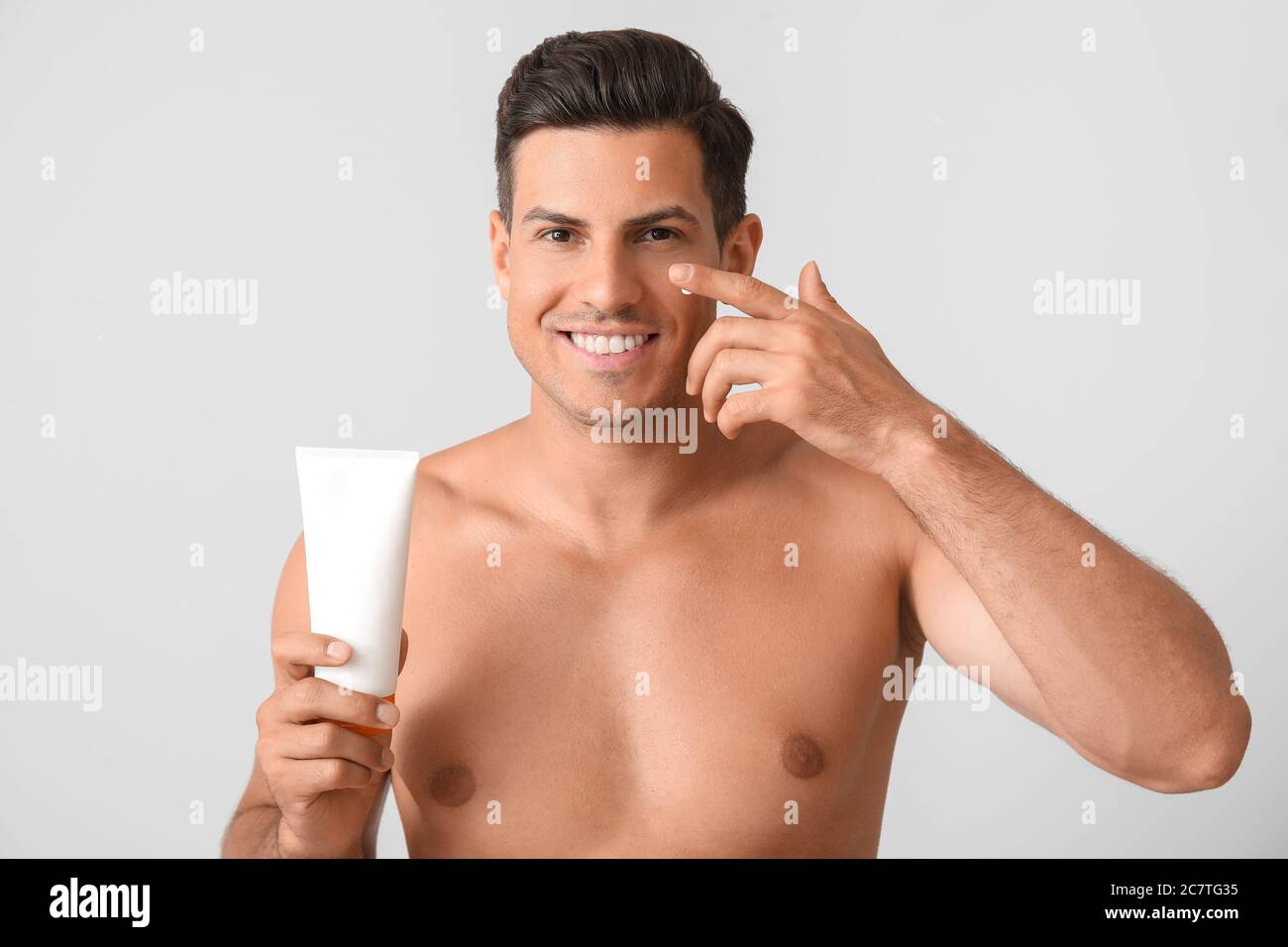 Young man applying sunscreen cream against light background Stock Photo ...