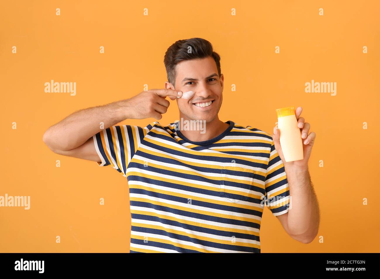 Young man applying sunscreen cream against color background Stock Photo ...