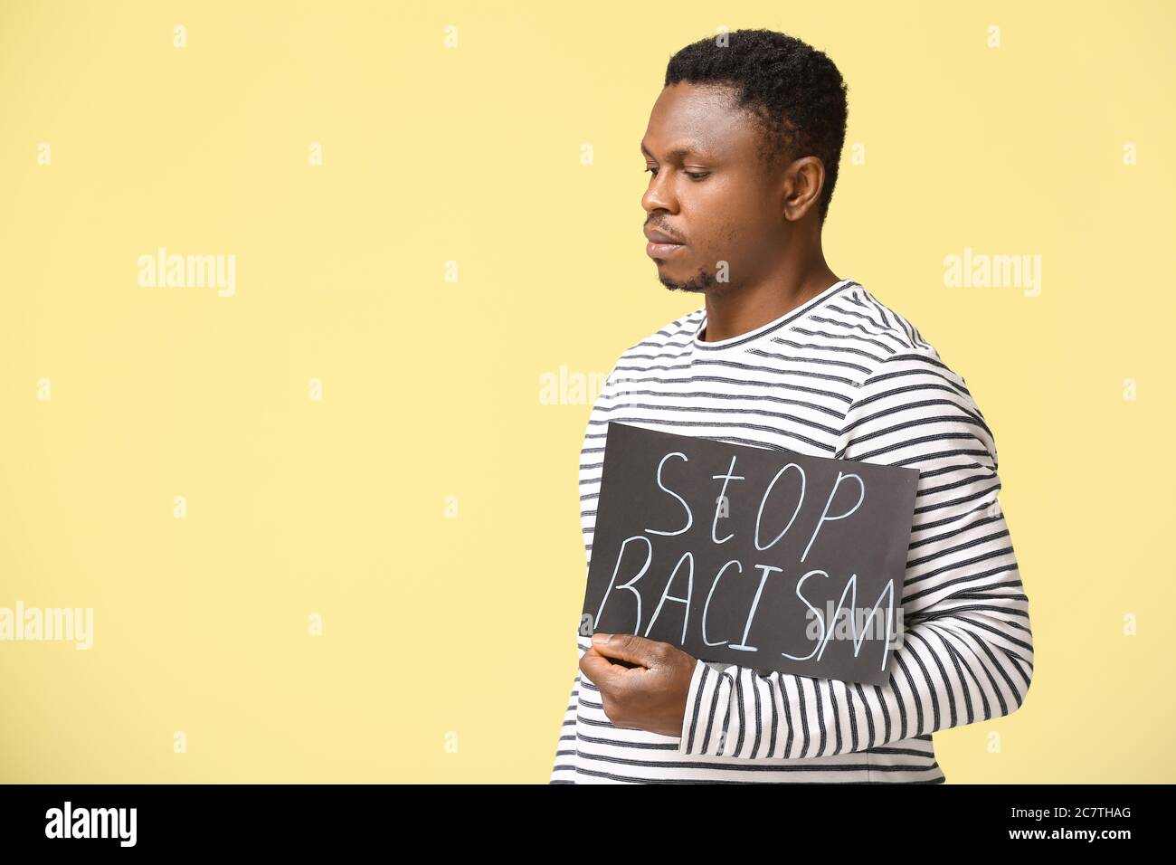 Sad African-American man with poster on color background. Stop racism ...