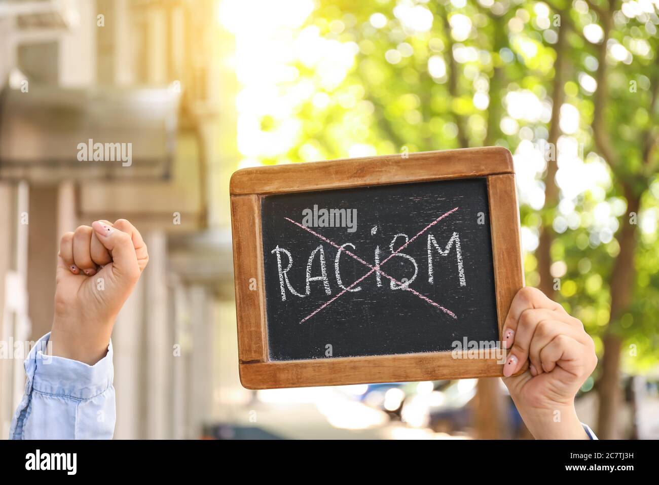 Woman holding chalkboard with crossed out word RACISM outdoors Stock ...