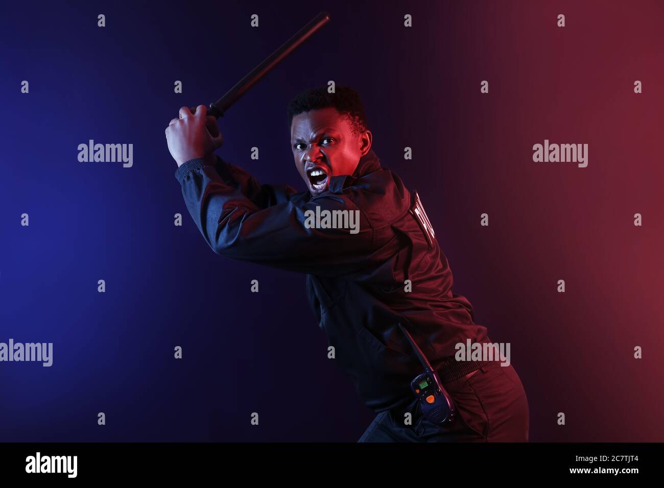 Aggressive African-American police officer with baton on dark color ...