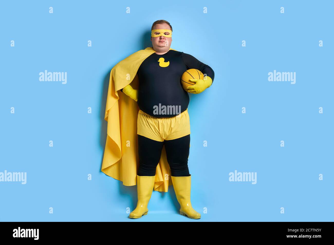 portrait of sportive fat superhero with ball isolated over blue ...