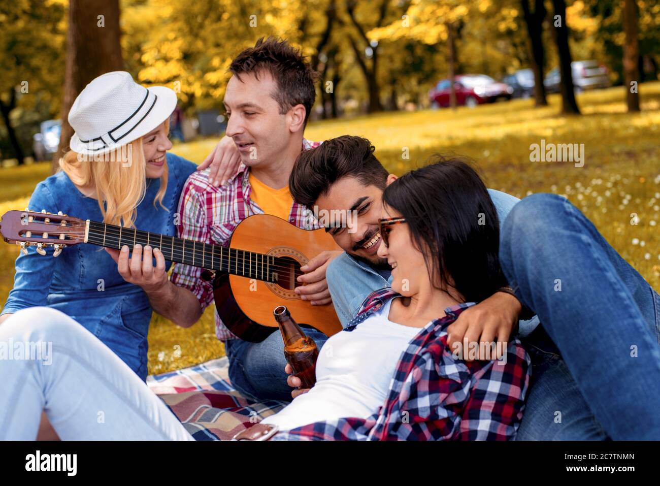 Group of young friends playing guitar and smiling on the grass in a ...