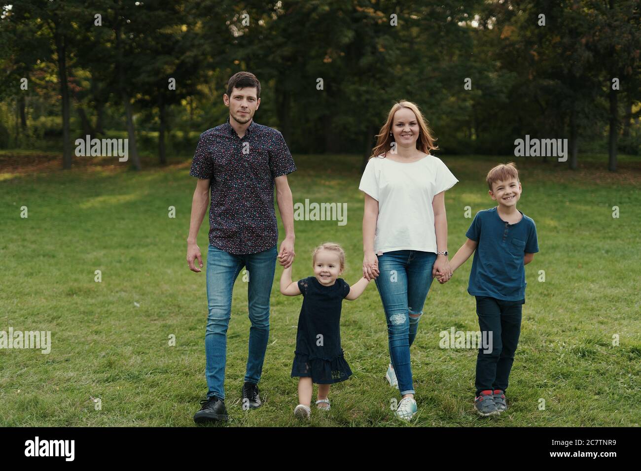 Four members family walks happily in the park holding hands and smiling ...