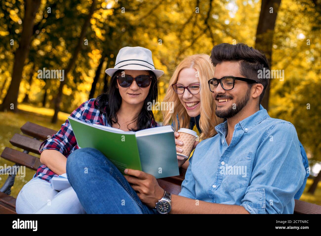Group of young friends reading a book and smiling on a park bench Stock ...