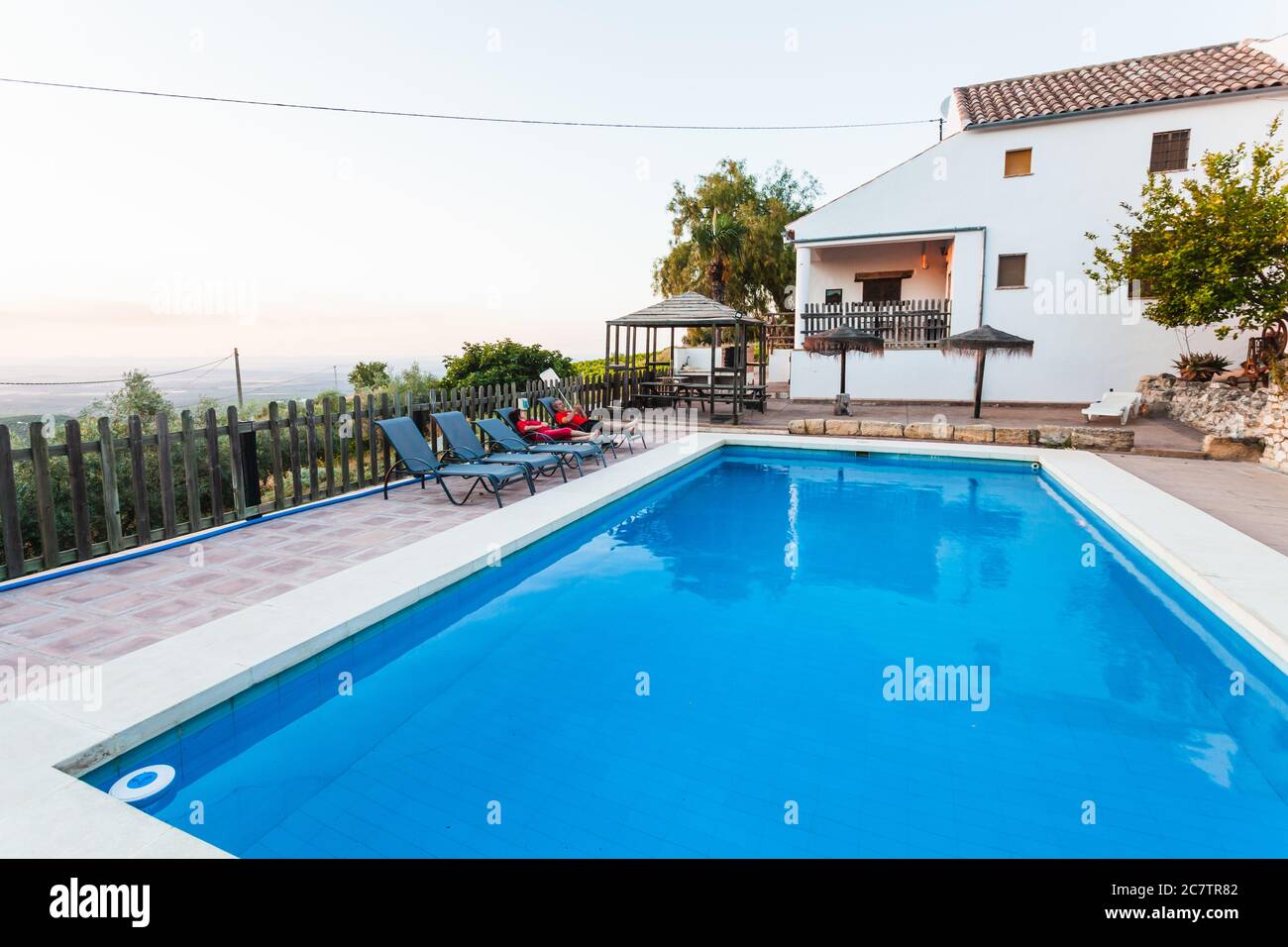 Outdoor pool with people resting on chairs on a side in the back of a ...