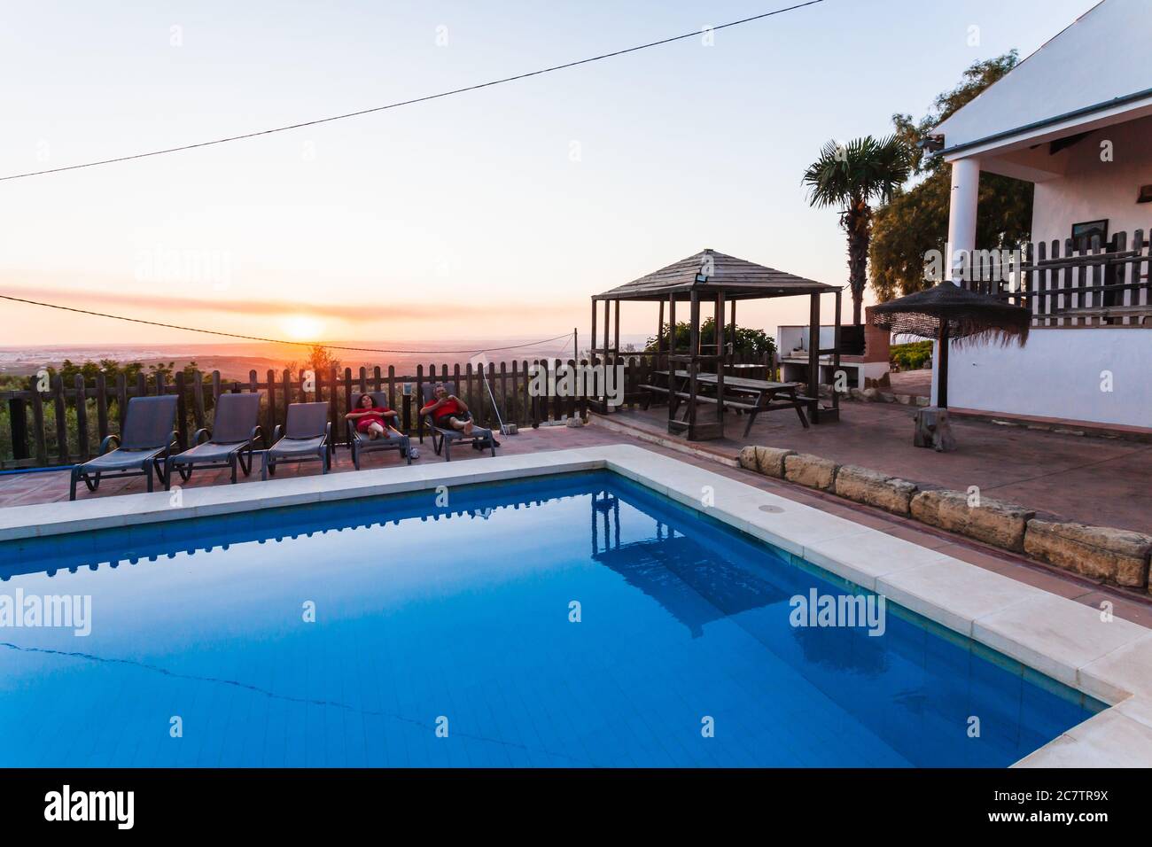 Outdoor pool with people resting on chairs on a side in the back of a ...