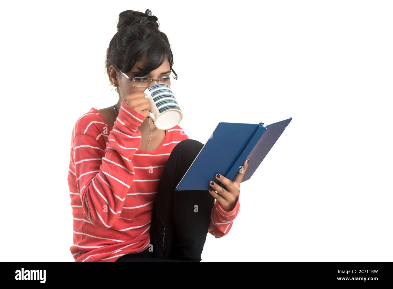 Beautiful young girl with book and cup of coffee posing on a white ...