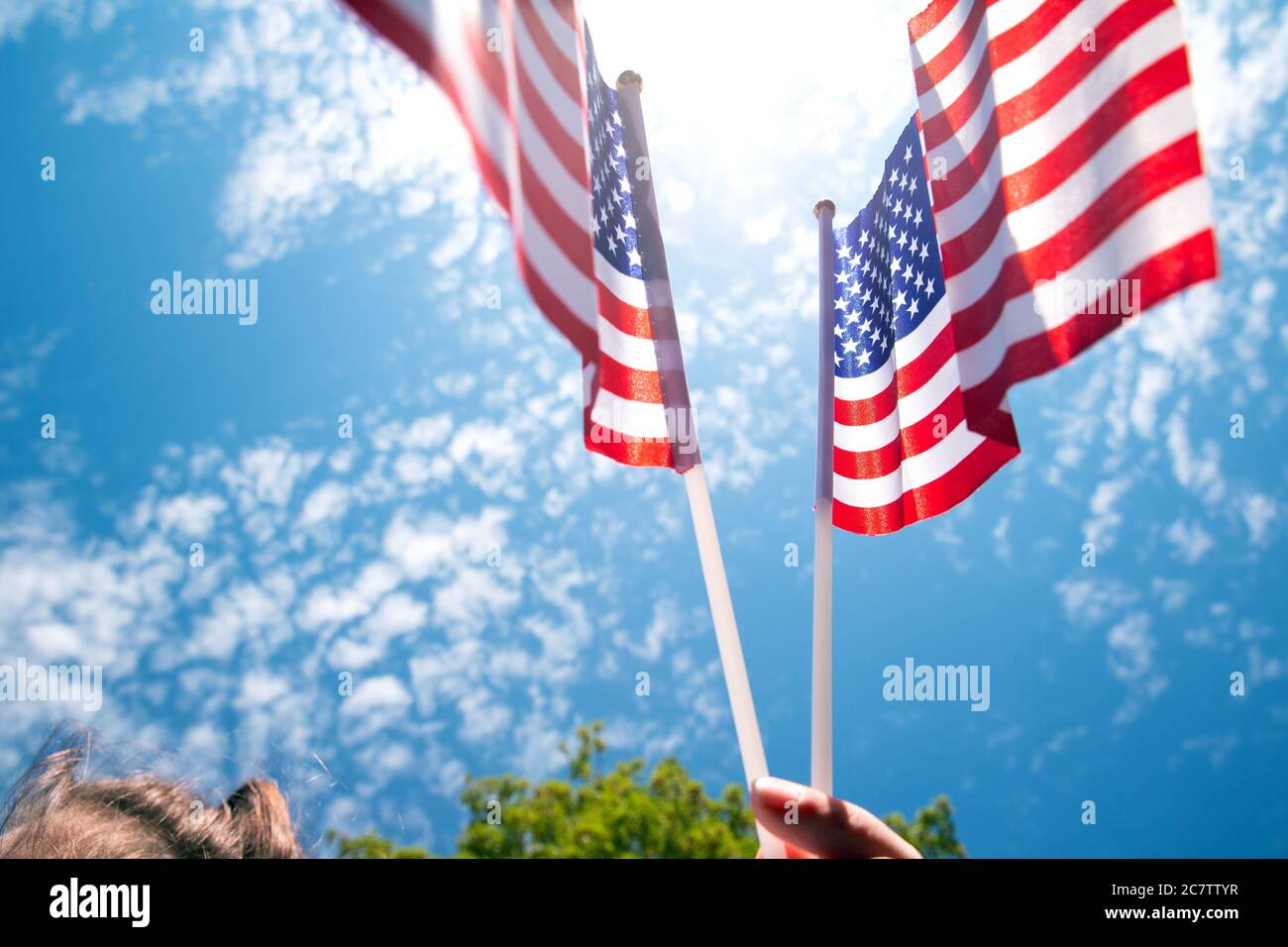Hand holding two american flags on the blue sky with sunlight ...