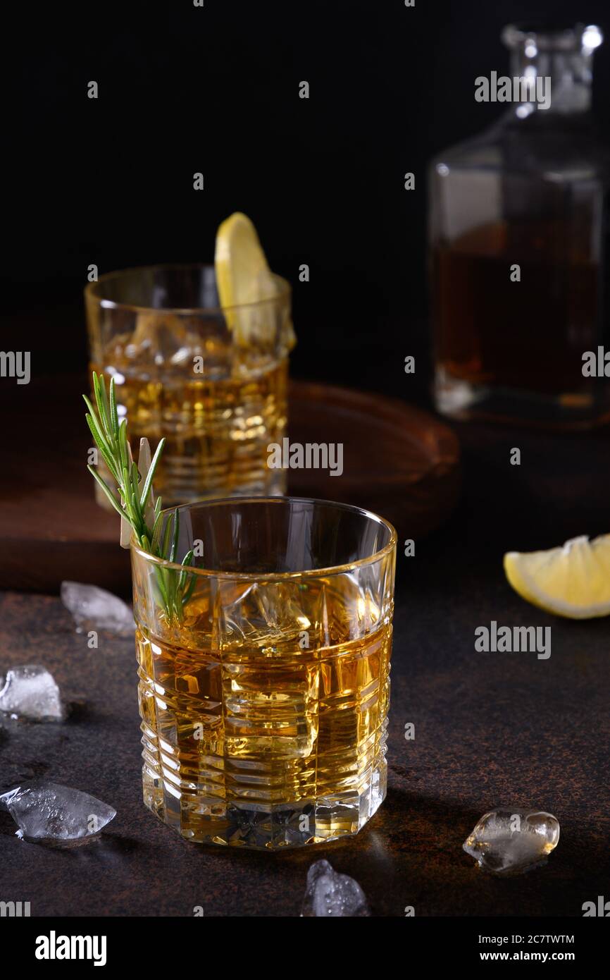 Three glasses of cold whiskey with rosemary, lemon peels on dark brown ...