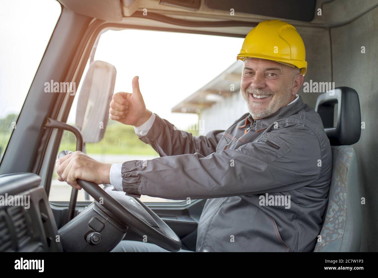 Happy male construction worker doing the thumbs-up gesture in a truck ...