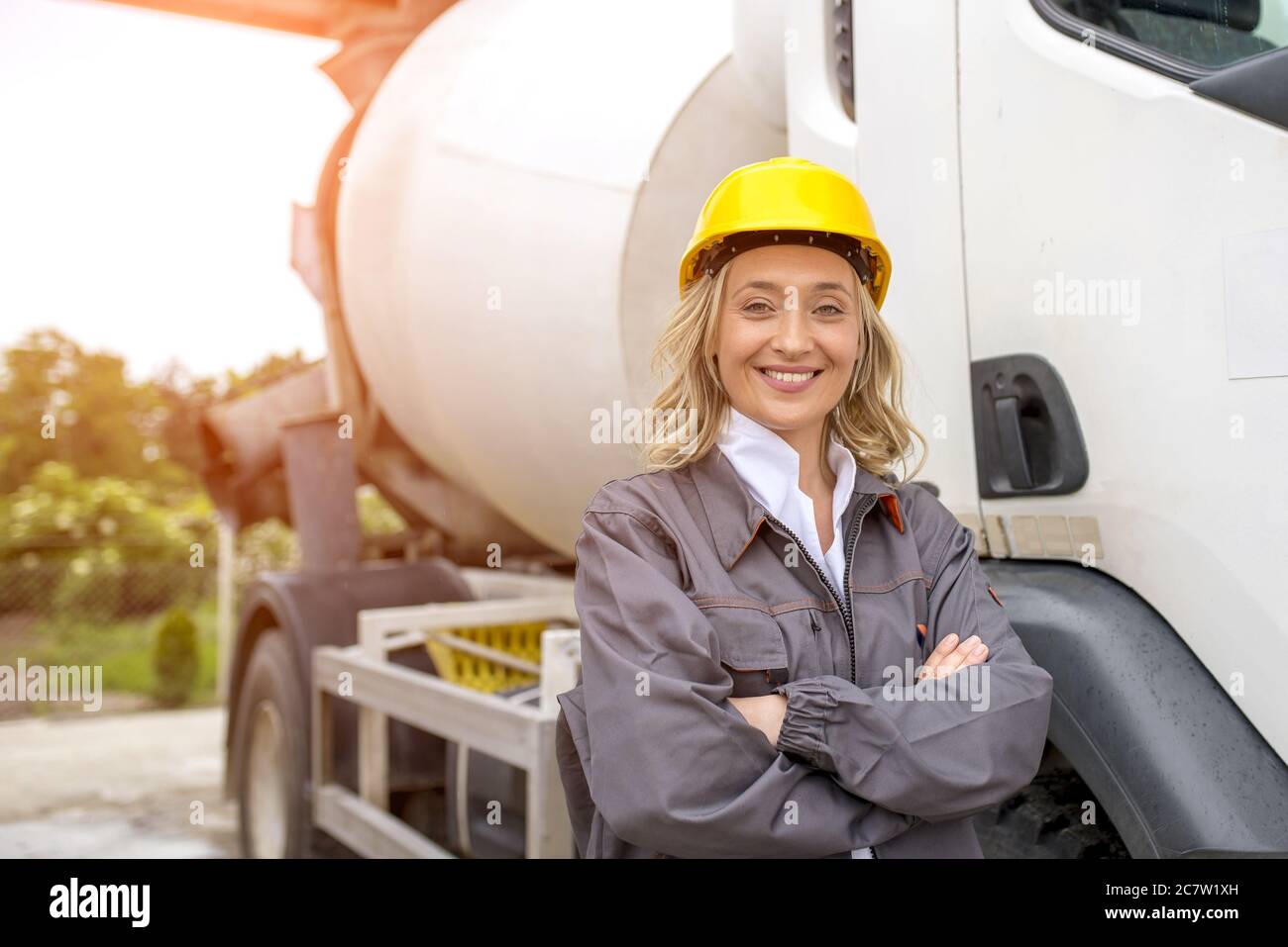 Happy female construction worker with folded arms standing near a truck ...