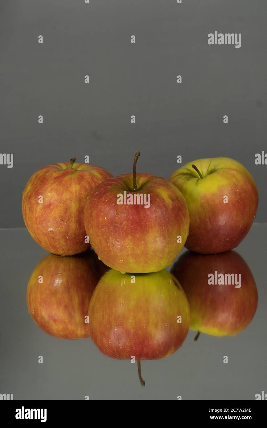 Three red apples on mirroring table on mirror gray background with ...
