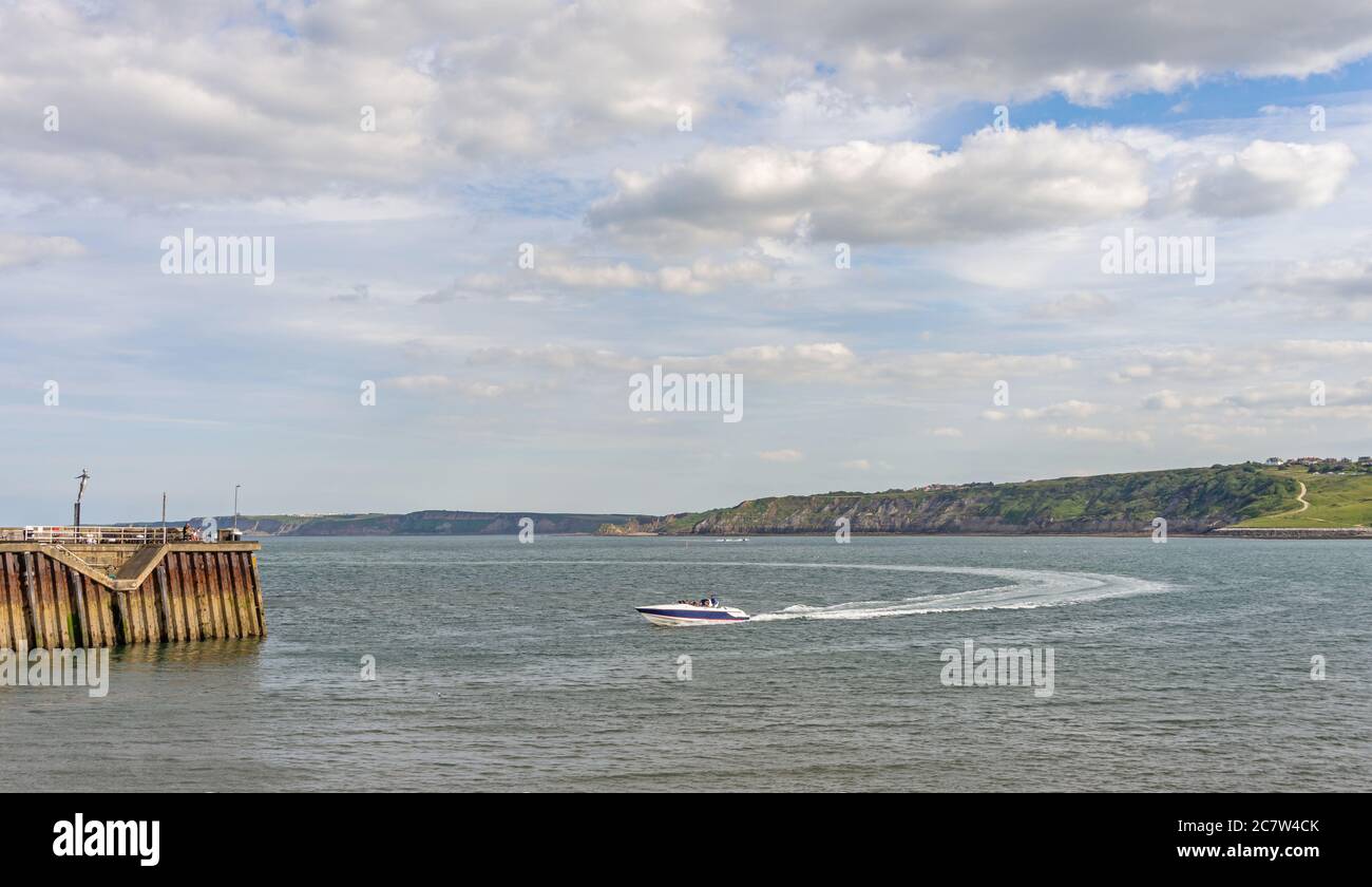 A speedboat approaches a pier leaving a curved wake behind it. A ...