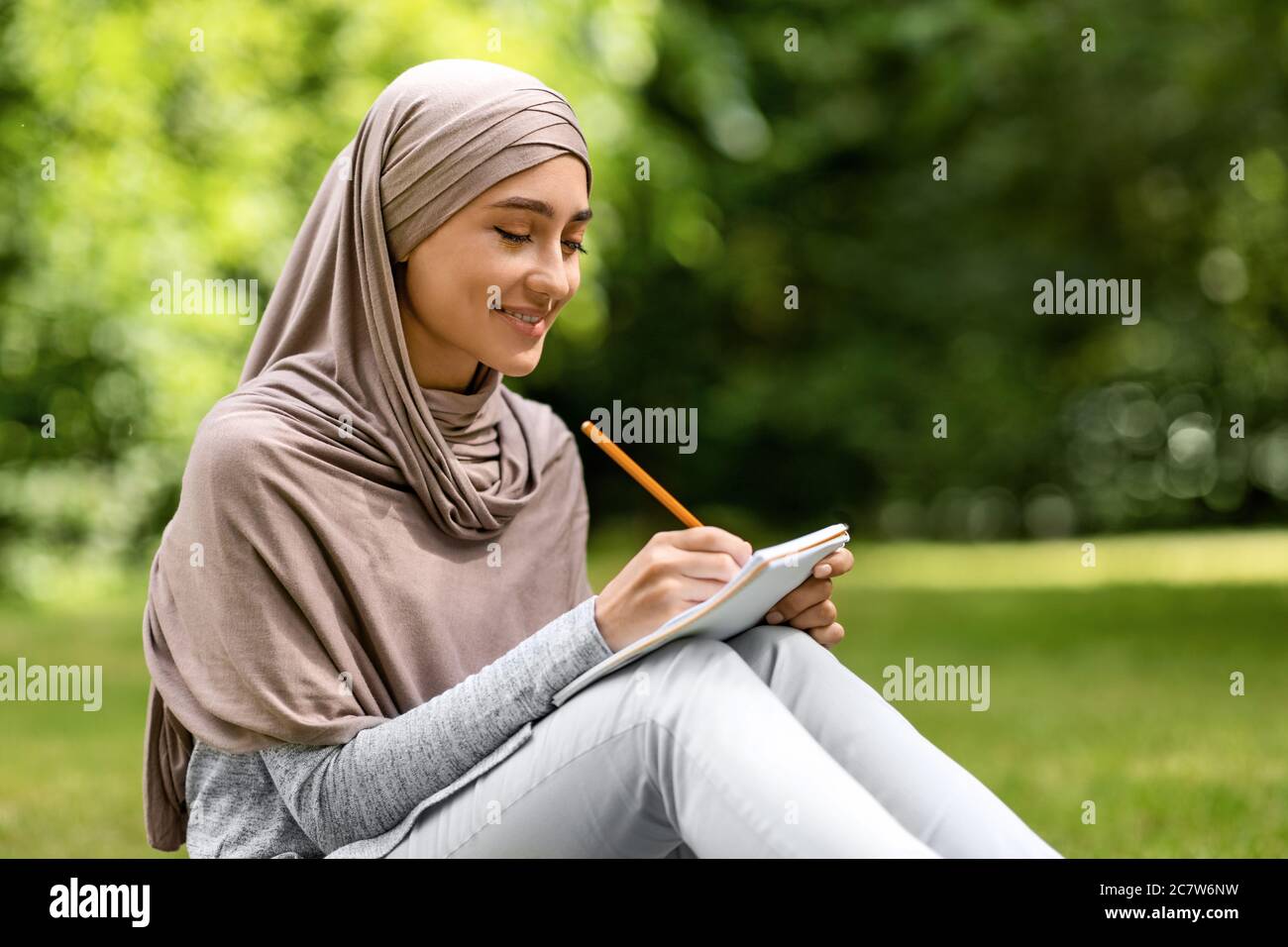 Girl in hijab writing on notebook, studying at public park Stock Photo ...