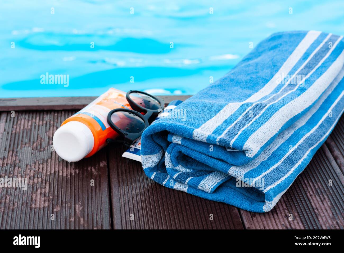 sun glasses, tube of sunscreen cream, blue towel near swimming pool ...