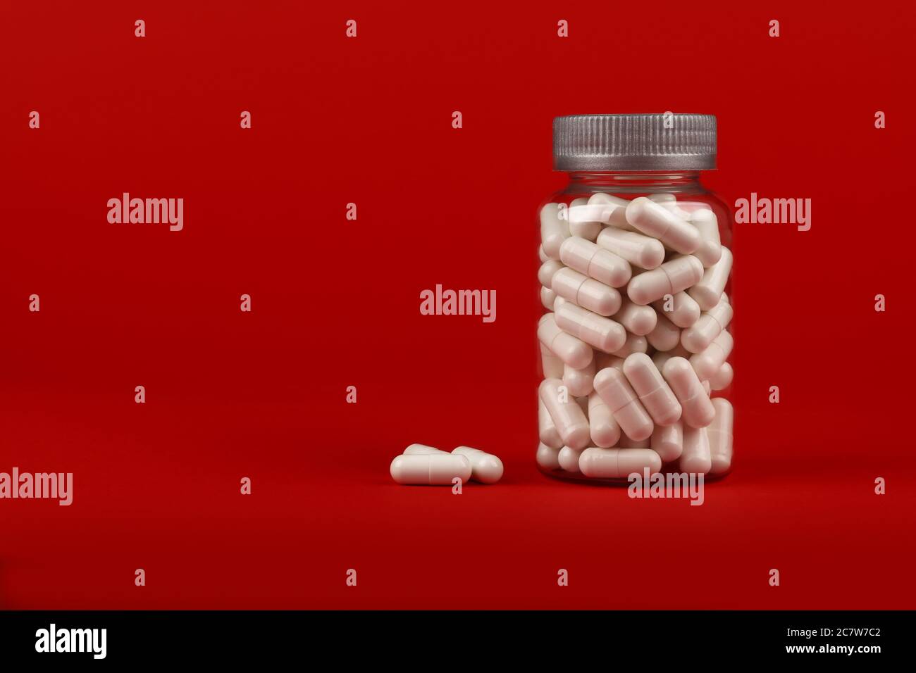 Close up one bottle of white gel cap pills of medicine over red ...